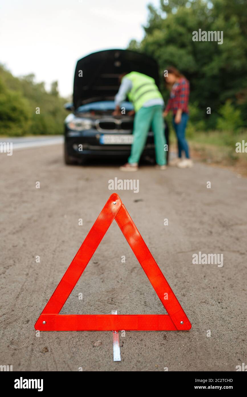 Emergency stop sign, young couple at the opened hood on road, car ...