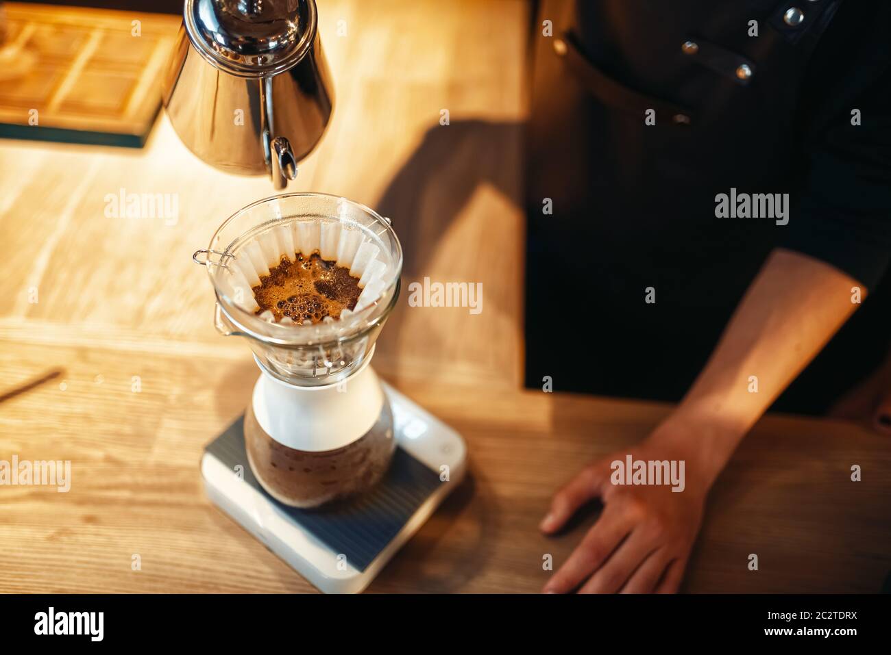Male barista pours hot water into the glass, latte preparation, wooden ...