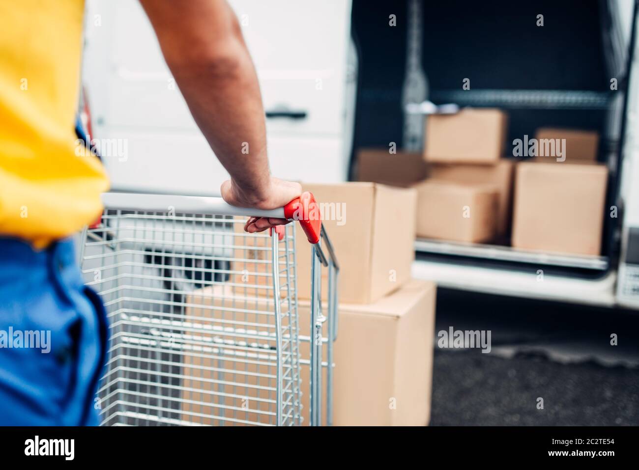 Male courier in uniform works with cargo, back view. Truck with parcels ...