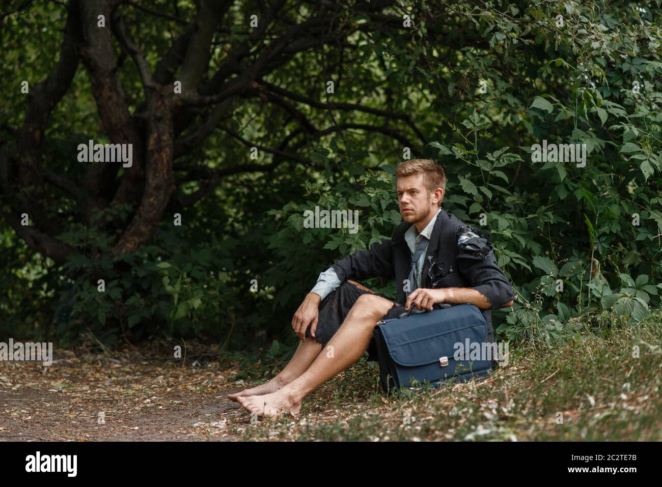 Businessman in torn suit sitting on the ground on desert island ...