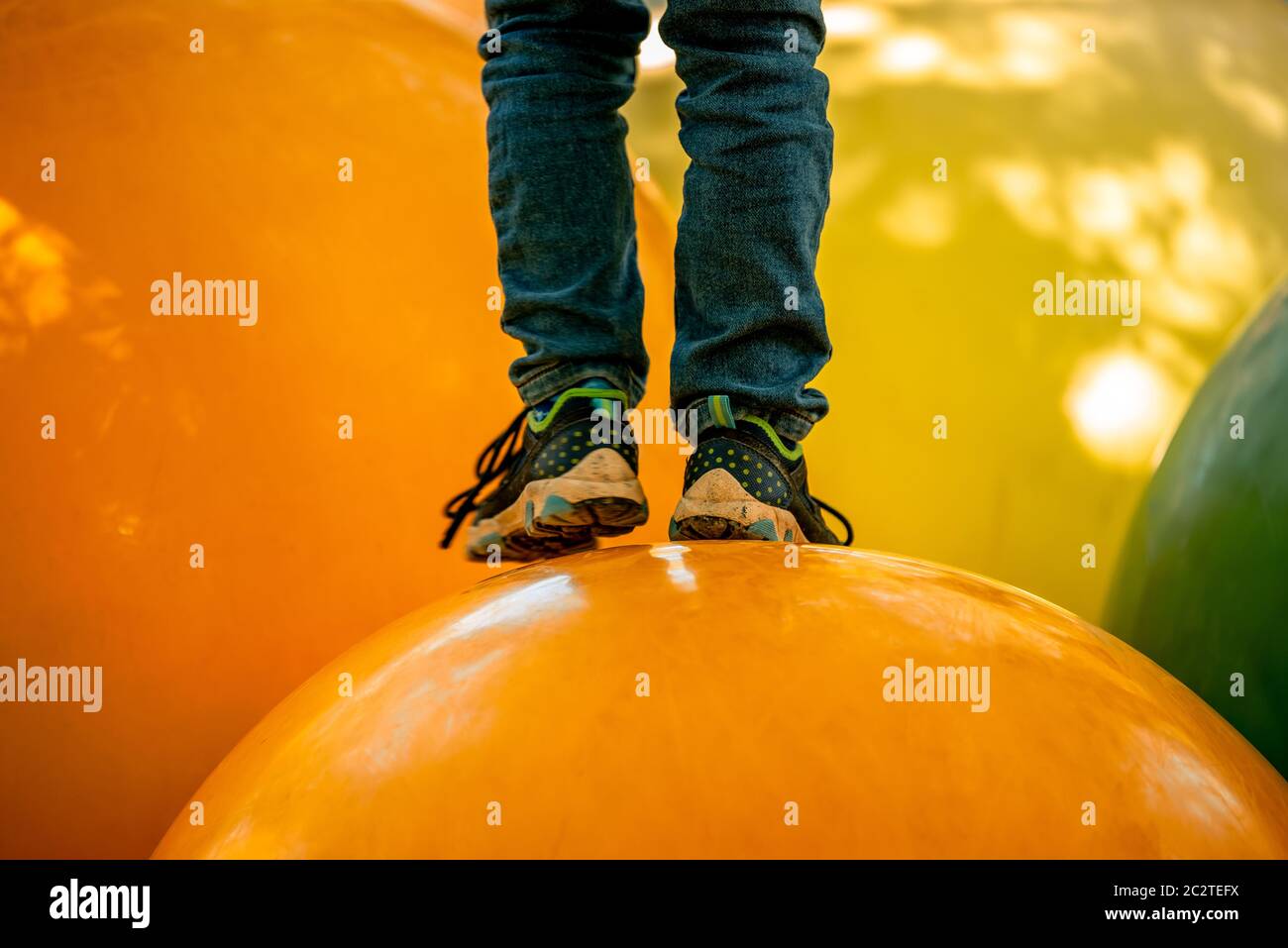 Baby, boy jumps on huge balls. Legs photographed from behind. Yellow ...