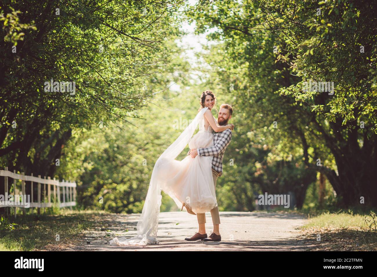 Happy bridegroom raises bride in summer park. man raised and hug woman ...
