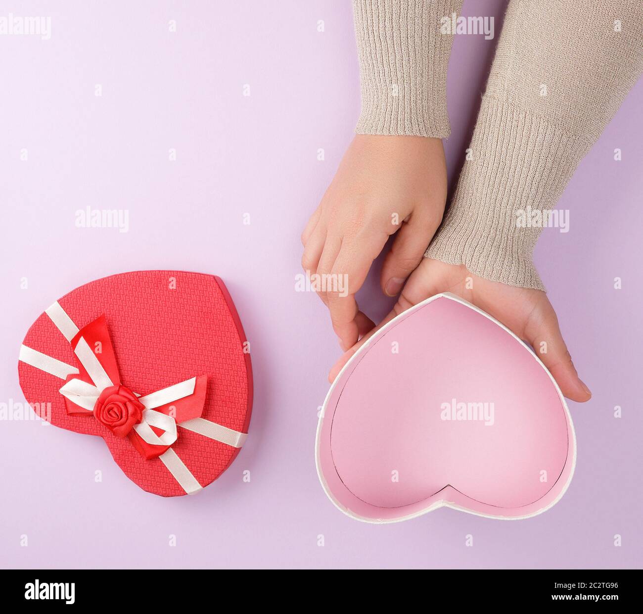 two hands hold a paper open red box in the shape of a heart on a purple ...