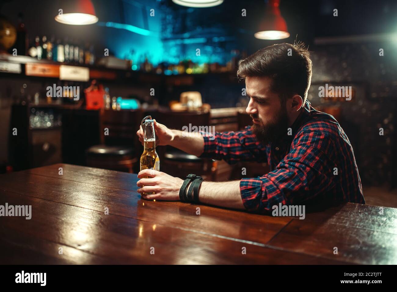 Sad man sitting at the bar counter and opens the bottle with alcohol ...