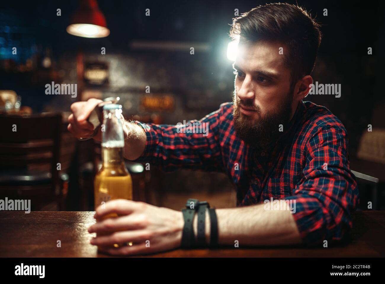 Sad man sitting at the bar counter and opens the bottle with alcohol ...