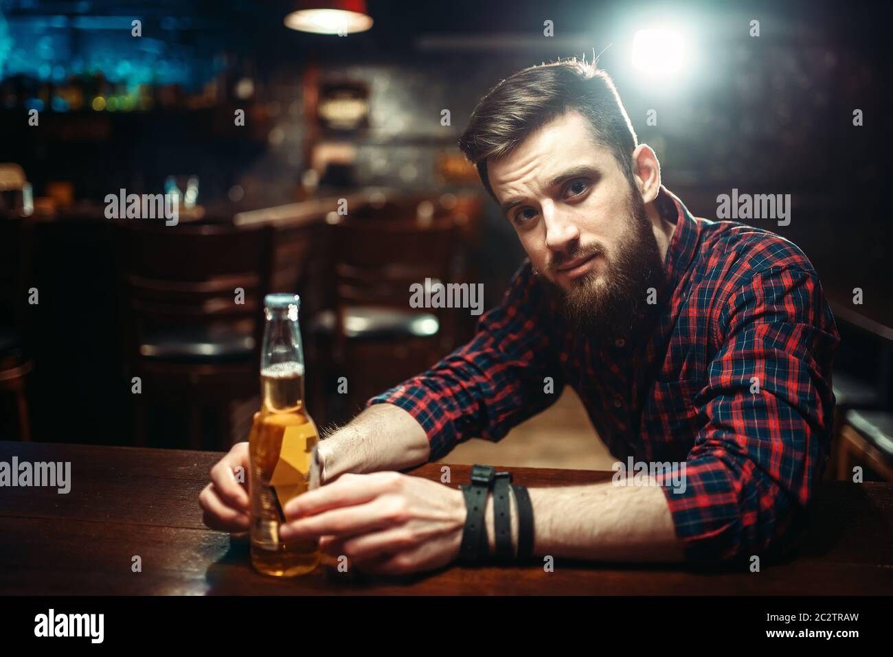 Sad man sitting at the bar counter and holds the bottle with alcohol ...