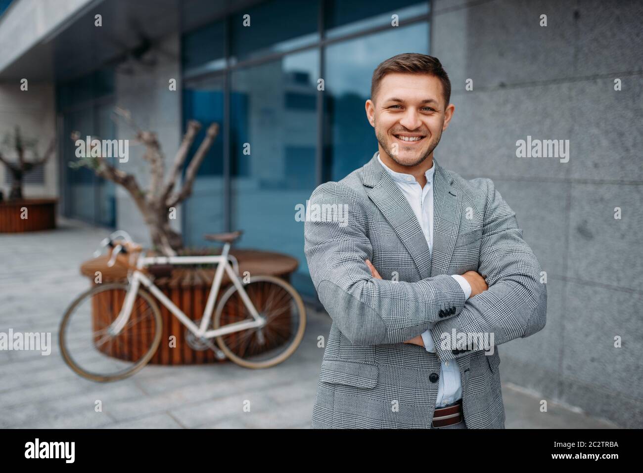 Smiling businessman with bicycle at the glass office building in ...