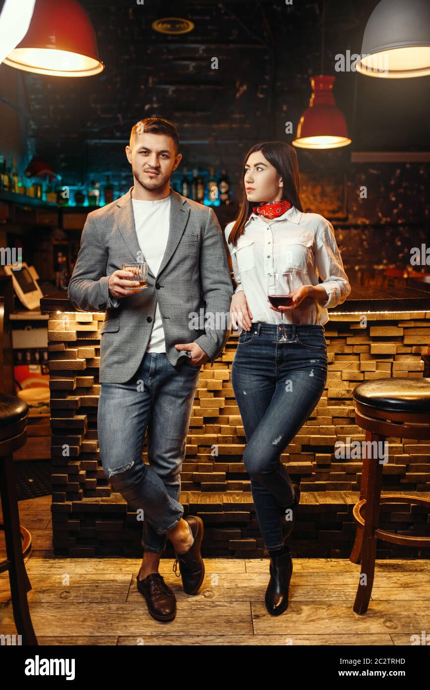 Love couple with alcoholic beverages standing against bar counter ...