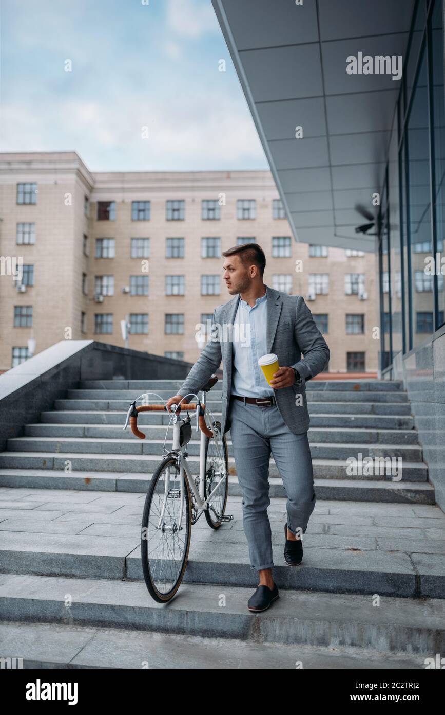 Businessman in suit with bicycle comes down the stairs at the office ...