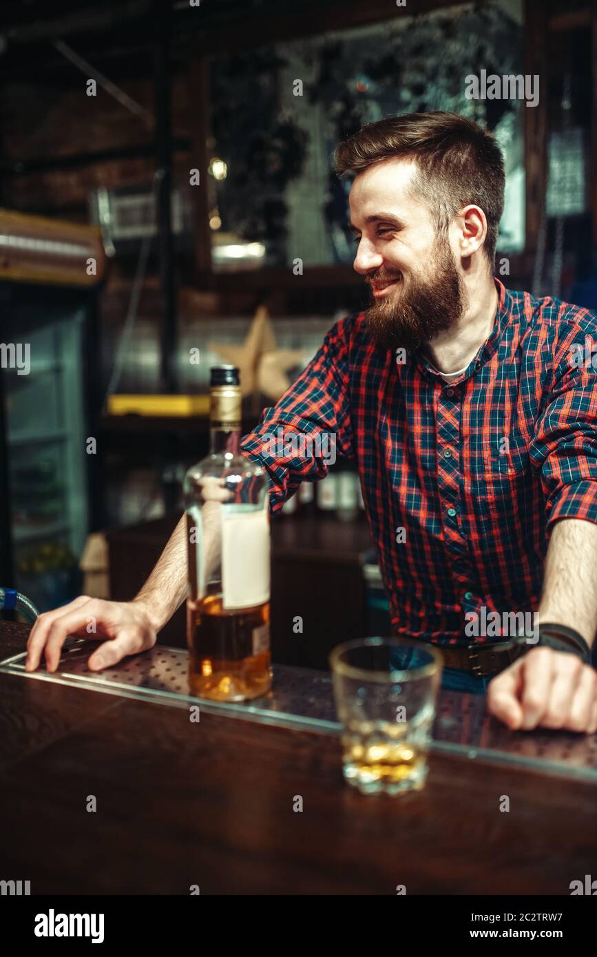 One man with bottle of alcohol beverage in hand standing at the bar ...