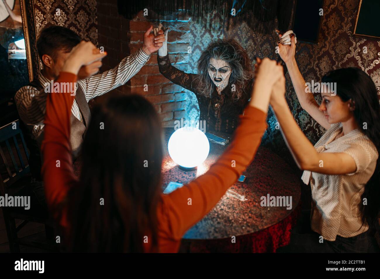 Scary witch reads a magic spell over a crystal ball, young people hands ...