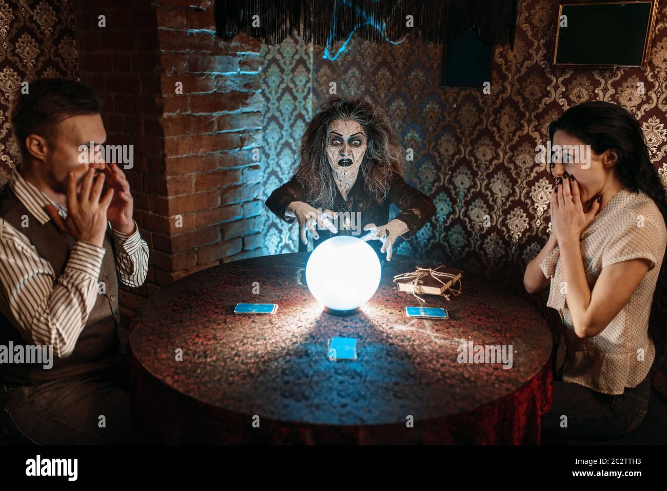 Witch reads scary magic spell over a crystal ball, young people in ...