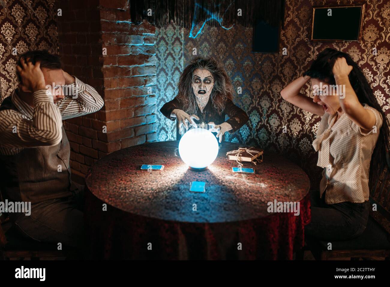 Witch reads scary magic spell over a crystal ball, young people in ...