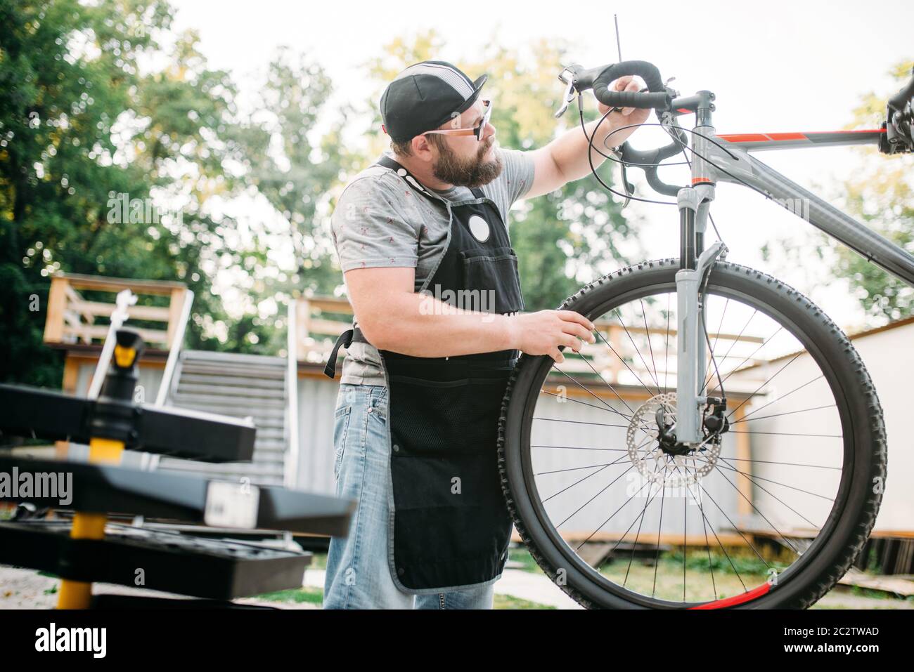 Professional bicycle mechanic in apron adjusts bike. Cycle workshop ...