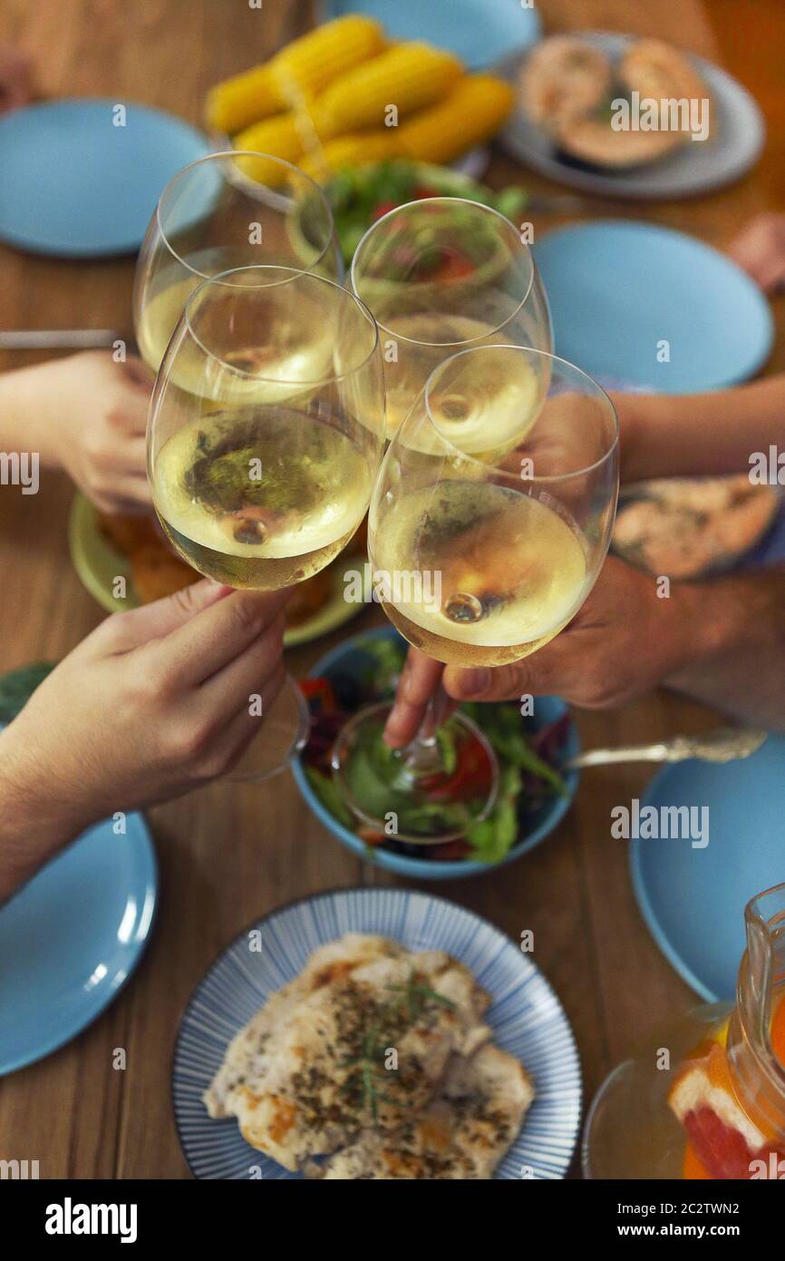 Hands of a group of people cheering with white wine and rising glasses ...
