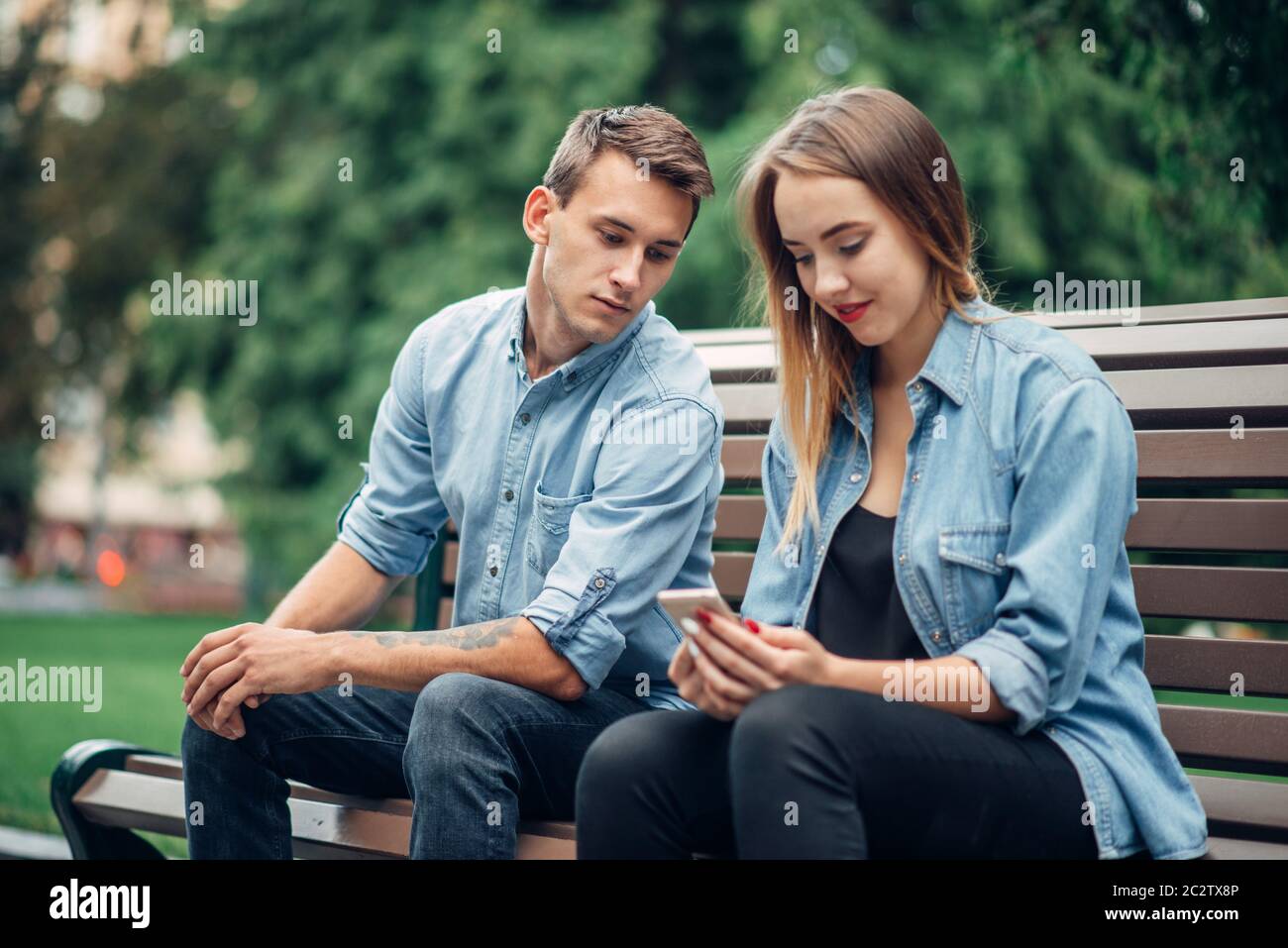 Phone addiction, young couple on the bench in park. Man and woman using ...