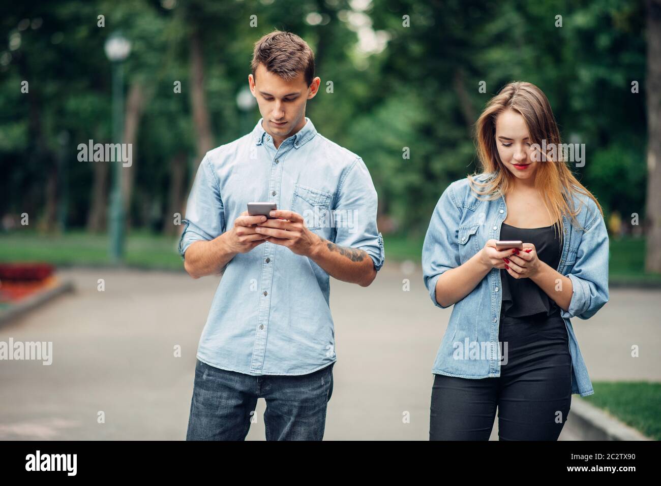 Phone addicted people, couple in summer park. Man and woman using their ...