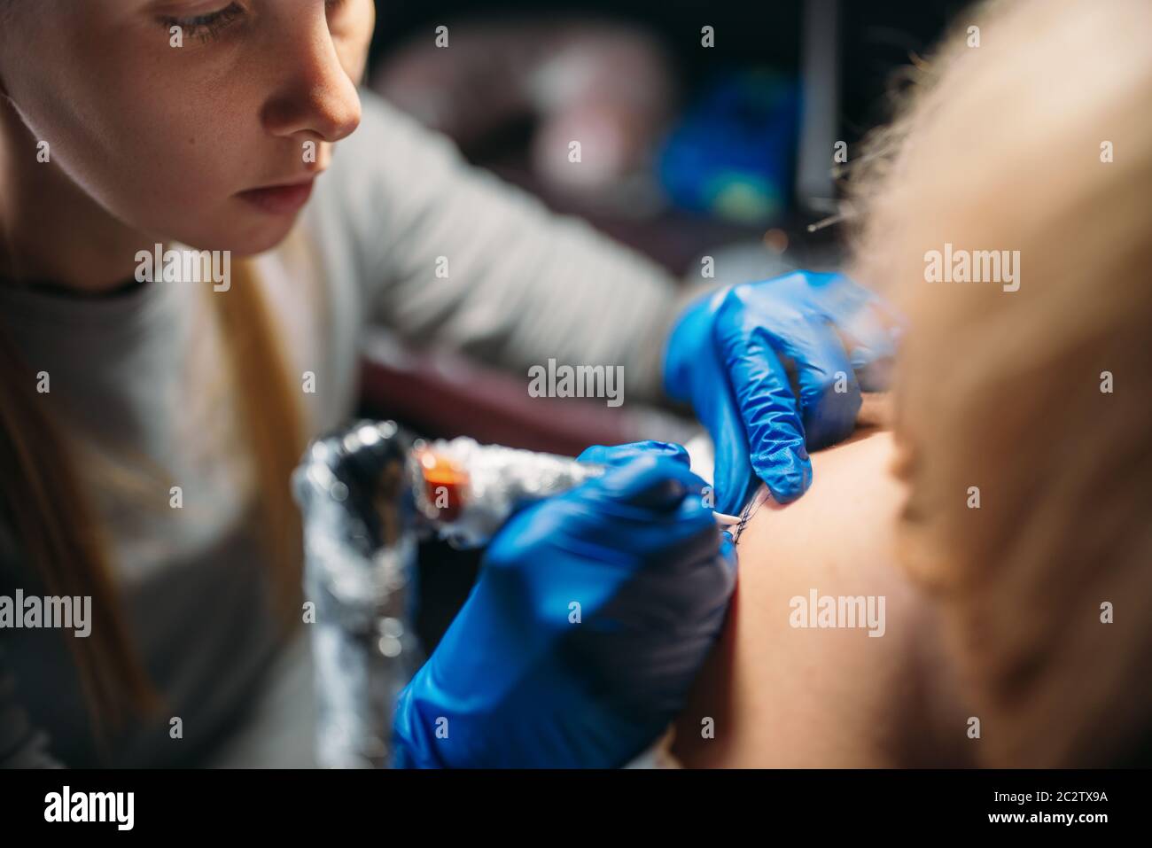 Female tattooist in blue sterile gloves makes tattoo by machine, master ...