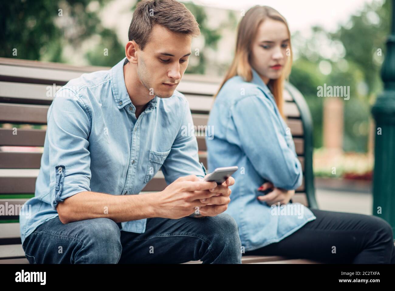 Phone addiction, young couple on the bench in park. Man and woman using ...