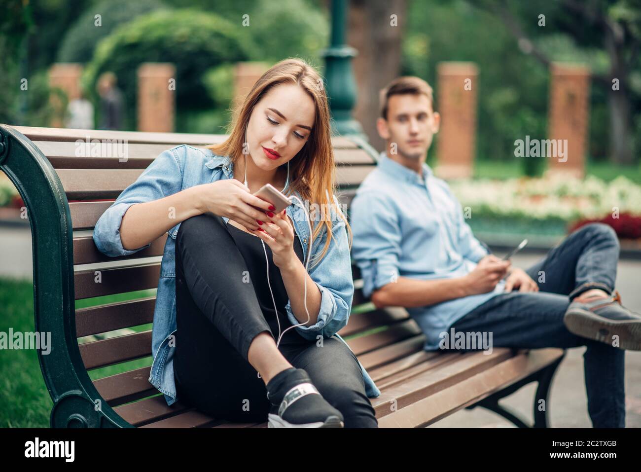 Phone addiction, smiling couple on the bench in park. Man and woman ...