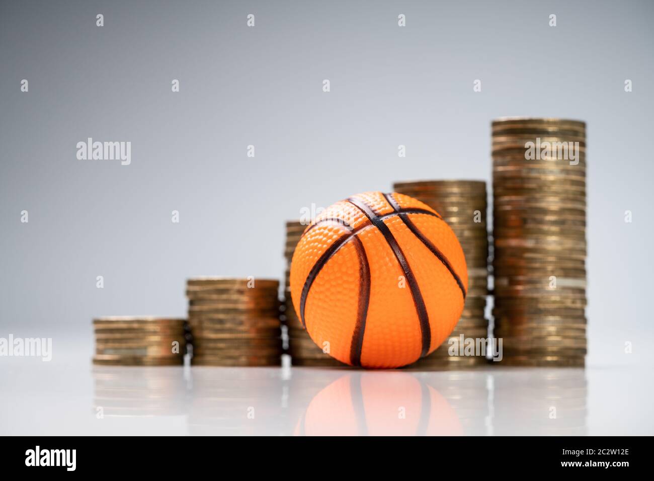 Miniature Basketball In Front Of Golden Coin Stacks On White Desk ...