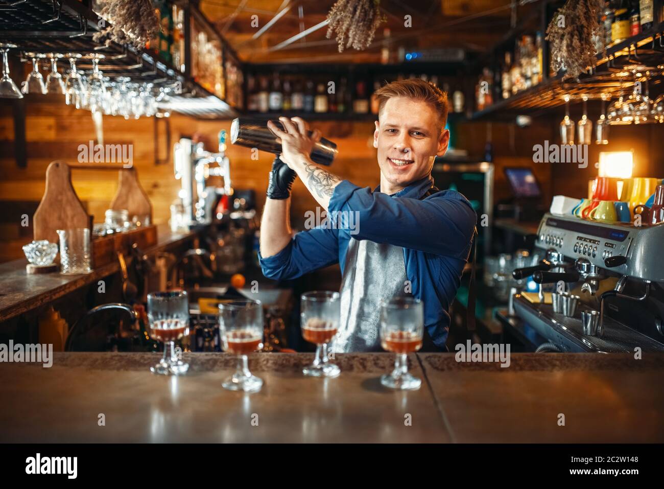 Male bartender in apron works with shaker at the bar counter. Alcohol ...