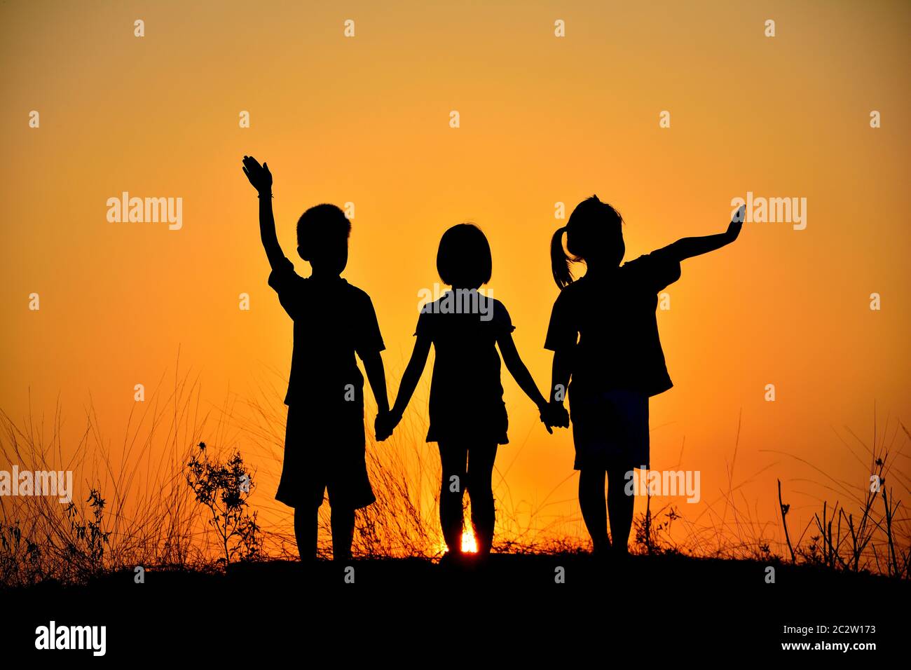 Black silhouette of three children standing together. There is a sky at ...