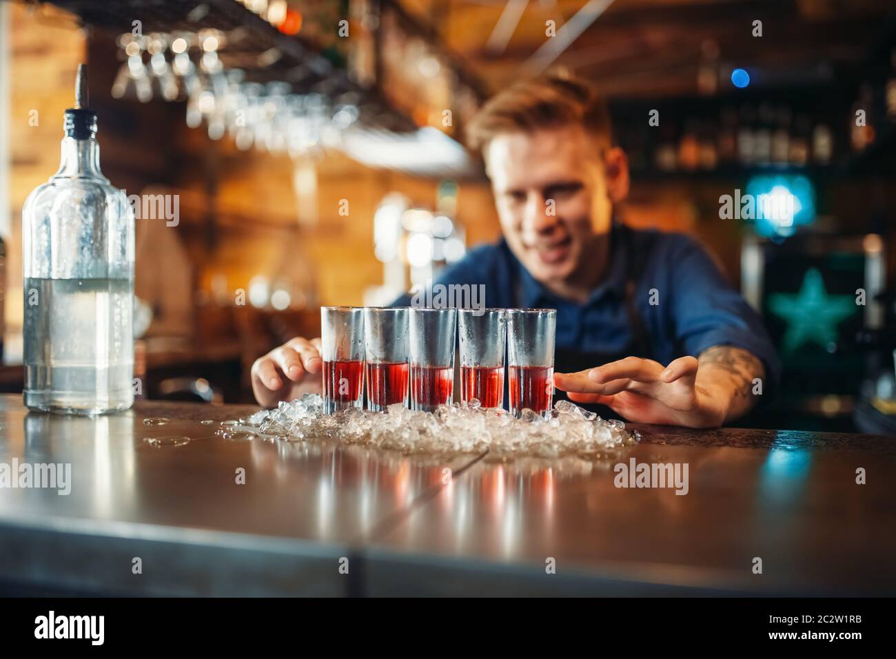 Male bartender in apron prepares four beverages in a glasses. Barman at ...