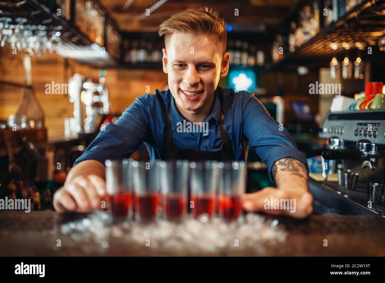 Male bartender in apron prepares four beverages in a glasses. Barman at ...