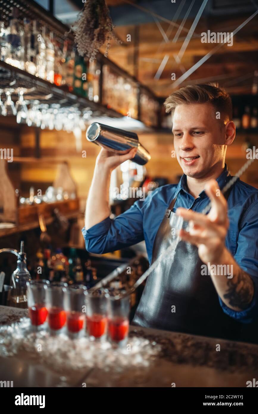 Male barman prepares alcoholic coctail, glasses standing in ice ...
