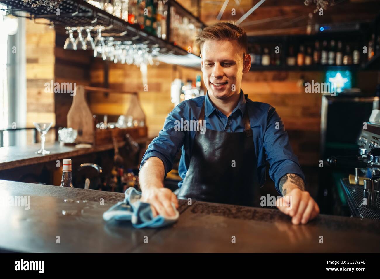 Male barman in apron cleans bar counter. Barkeeper occupation ...