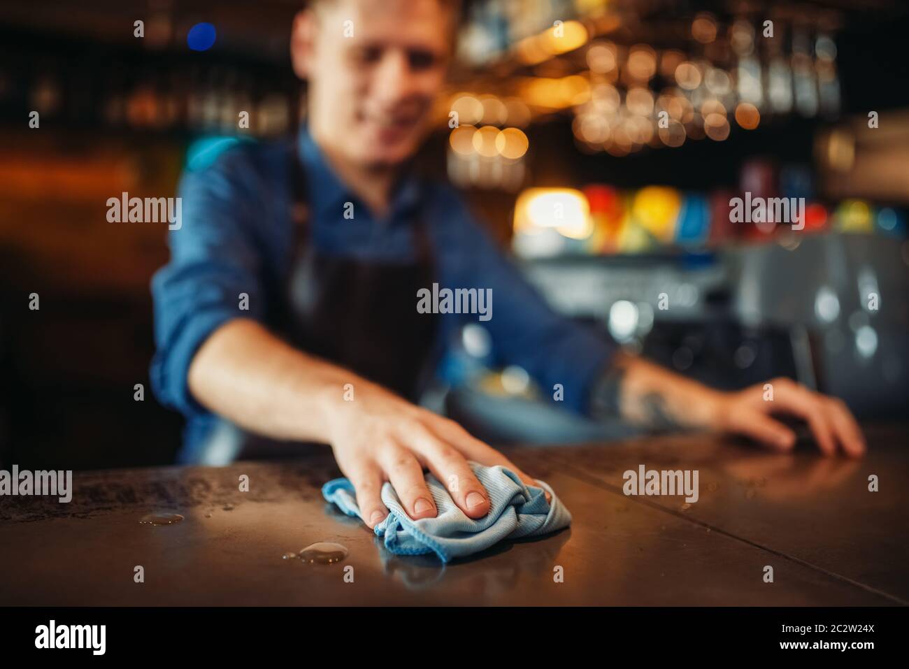 Male barman in apron cleans bar counter. Barkeeper occupation ...