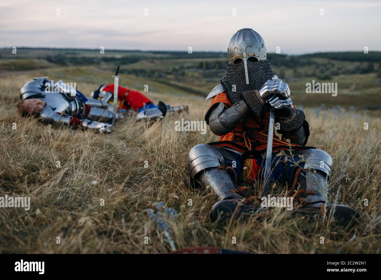 Medieval knight in armor and helmet sitting on the ground after great ...