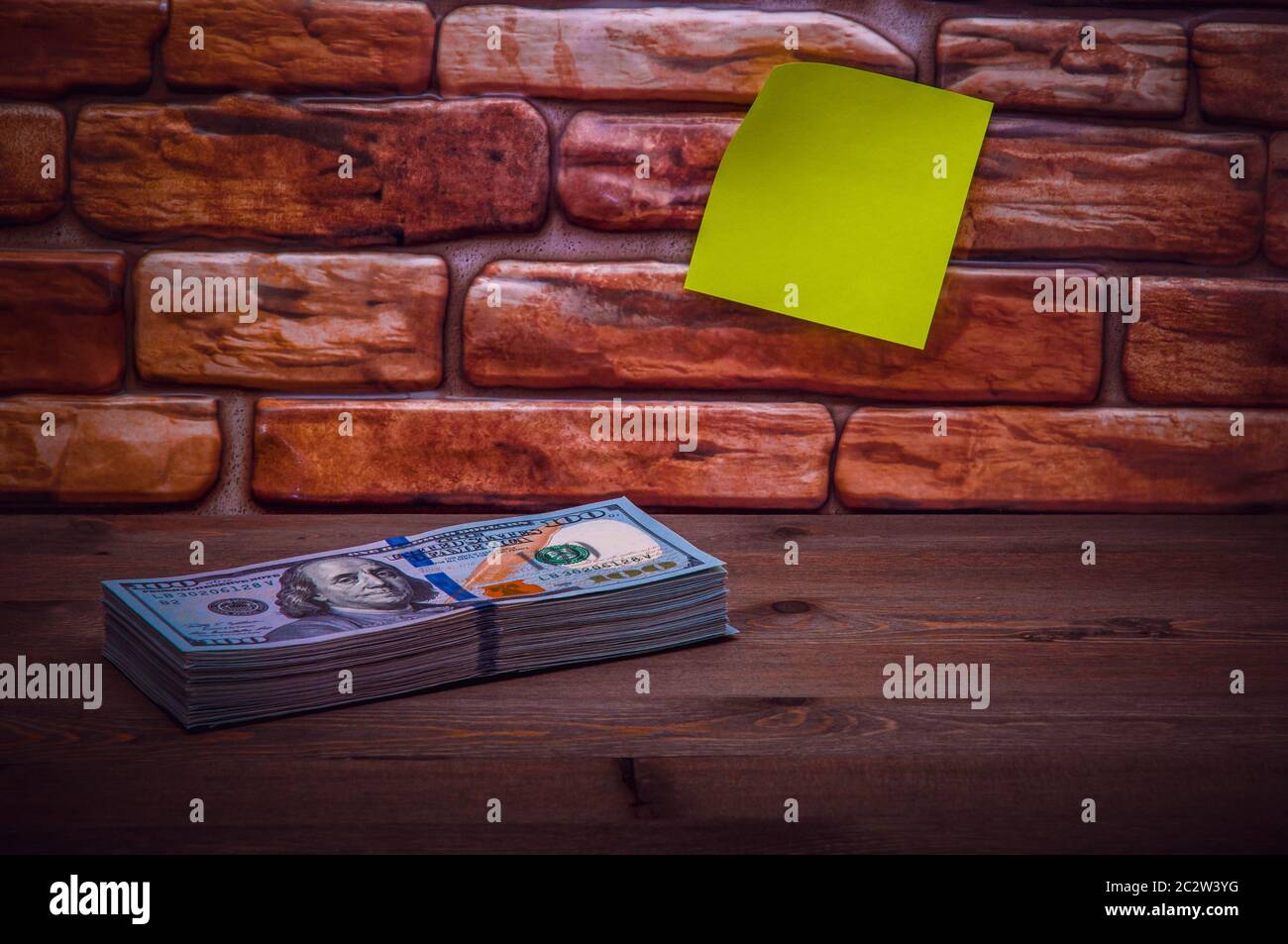 A stack of hundred-dollar bills against a brick wall and a note Stock ...