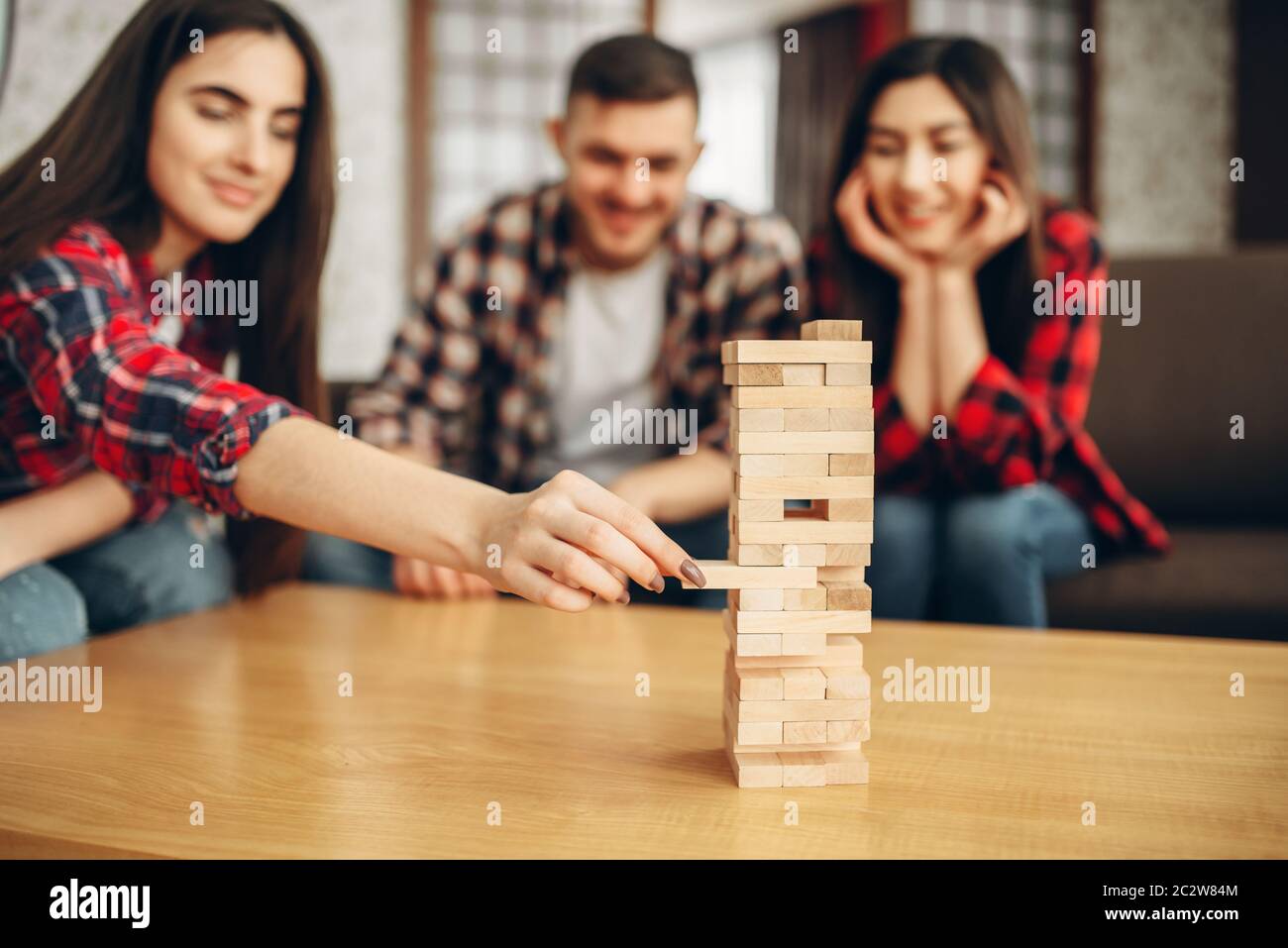 Smiling friends plays jenga at home, selective focus on tower. Board ...