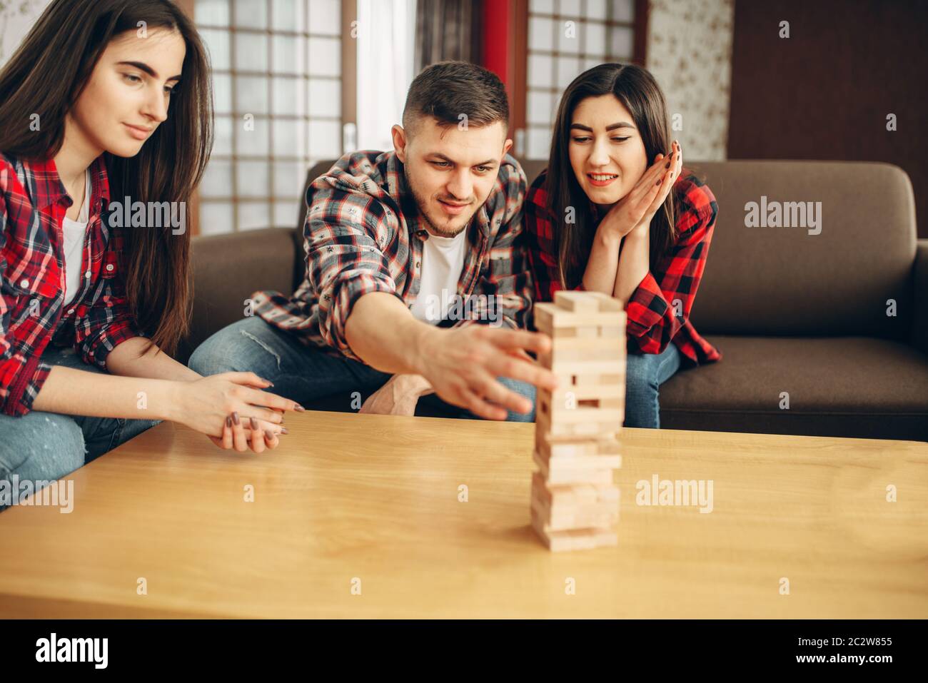 Smiling friends plays jenga at home, selective focus on tower. Board ...