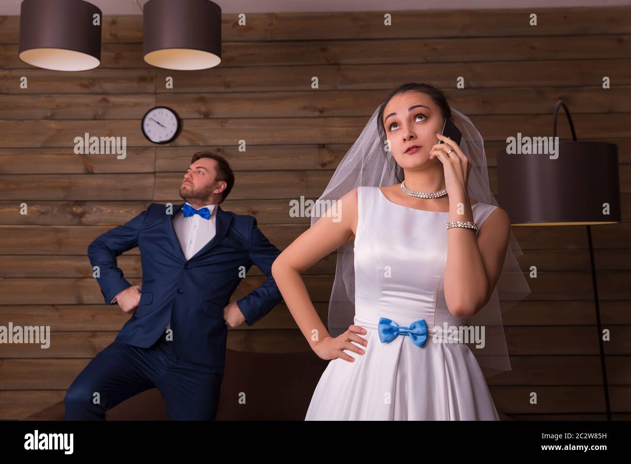 Portrait of bride using mobile phone and groom posing on camera, wooden ...