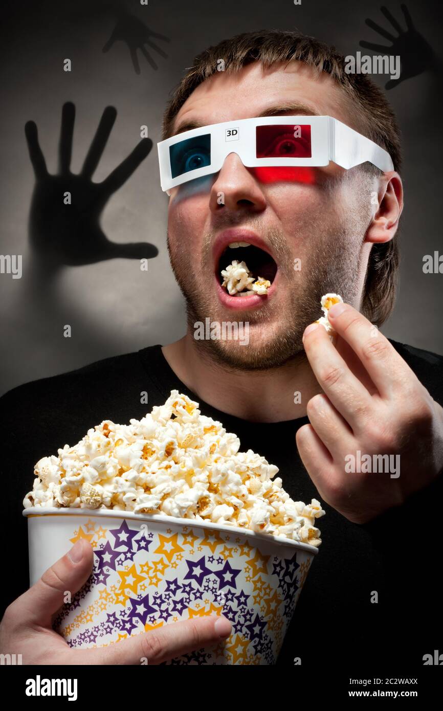 Portrait of scared man watching 3D movie and eating popcorn with dark ...
