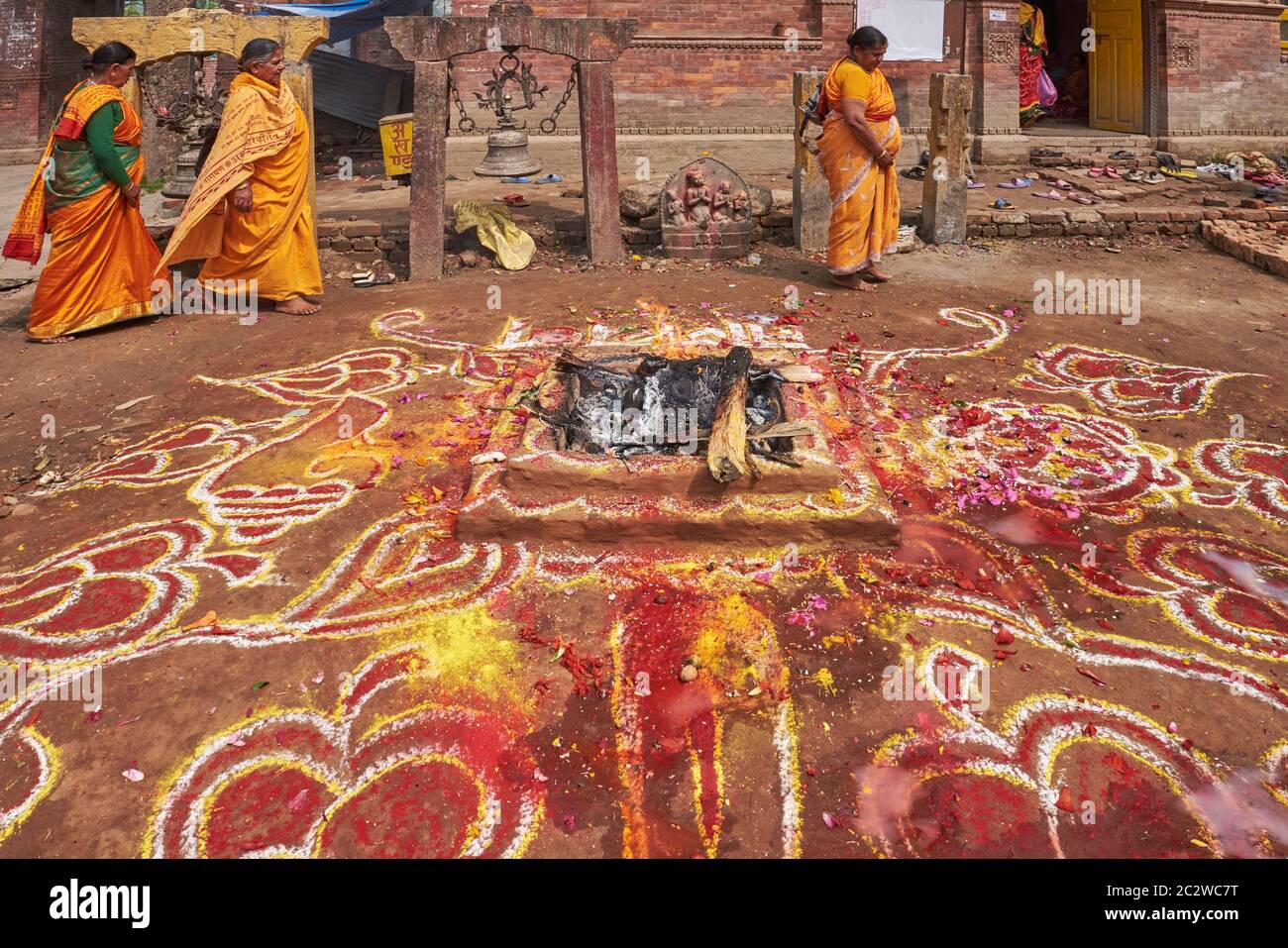 Sari-clad female temple visitors walk past the embers of a holy fire ...