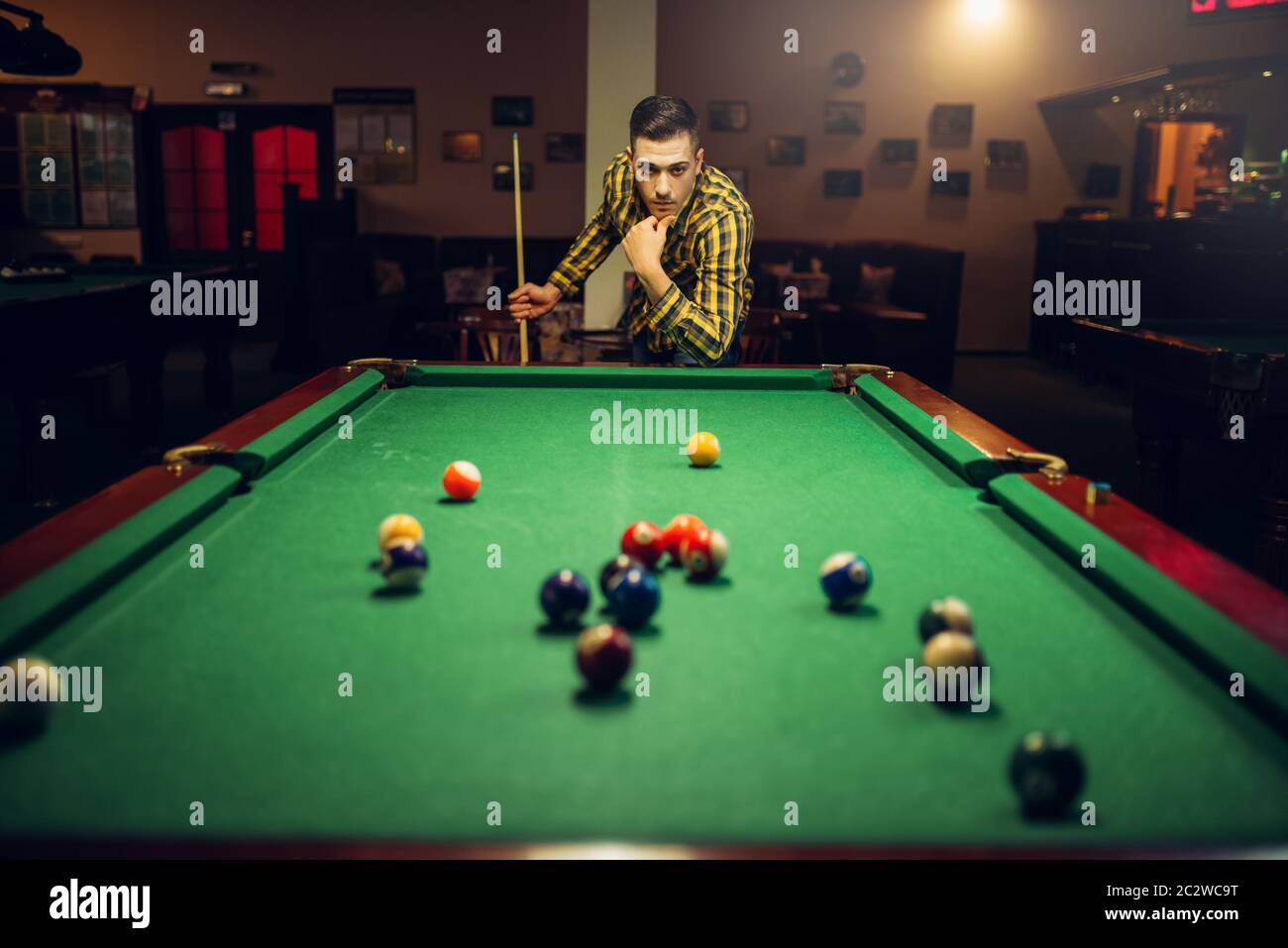 Male billiard player with cue thinking how to hit at the table with ...
