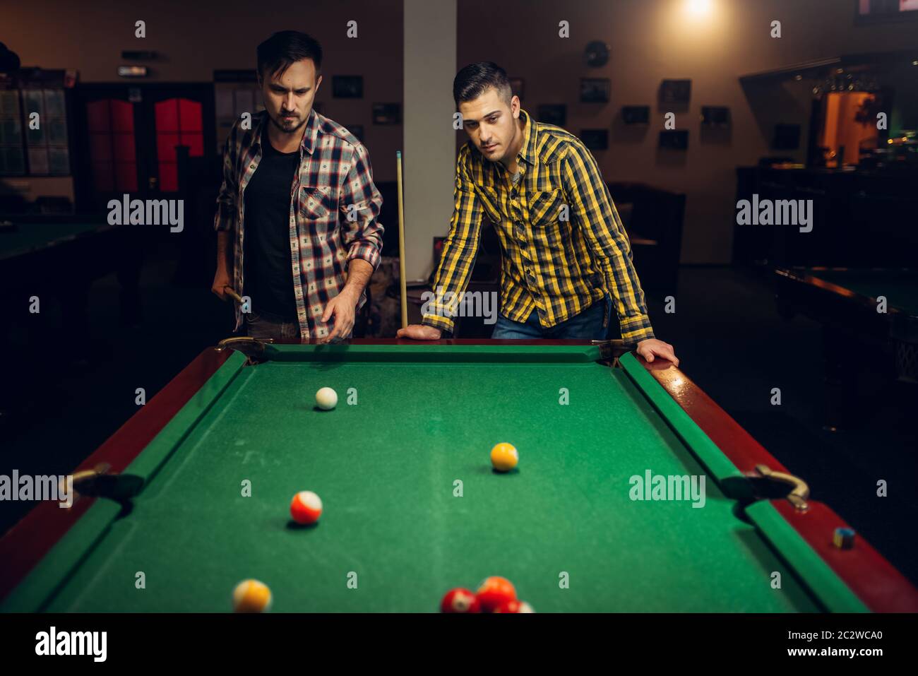 Two male billiard players with cue at the table with colorful balls ...