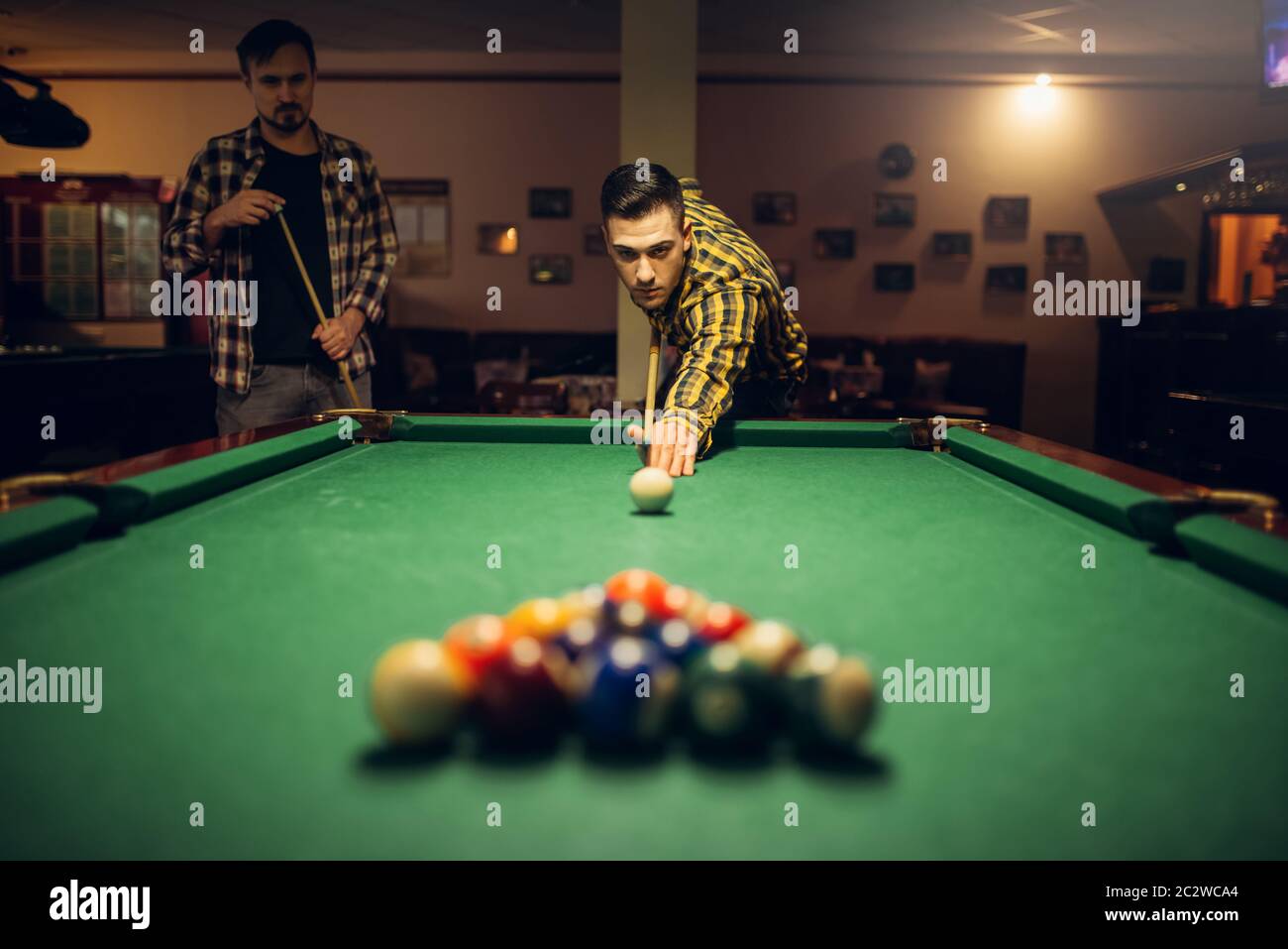 Male billiard player with cue aiming at the table with colorful balls ...