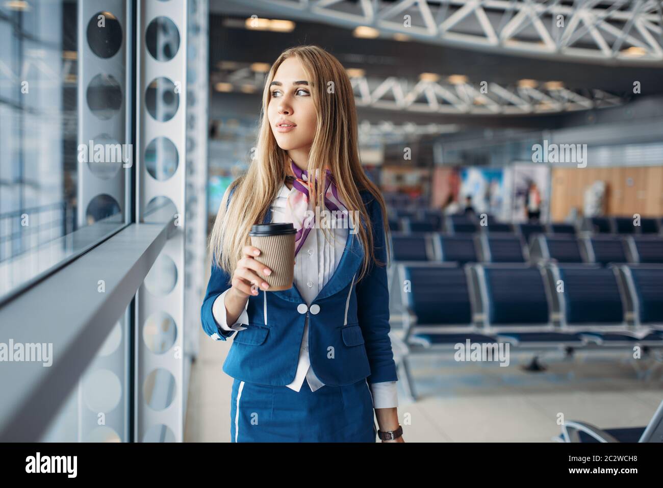 Stewardess with suitcase and coffee against window in airport. Air ...