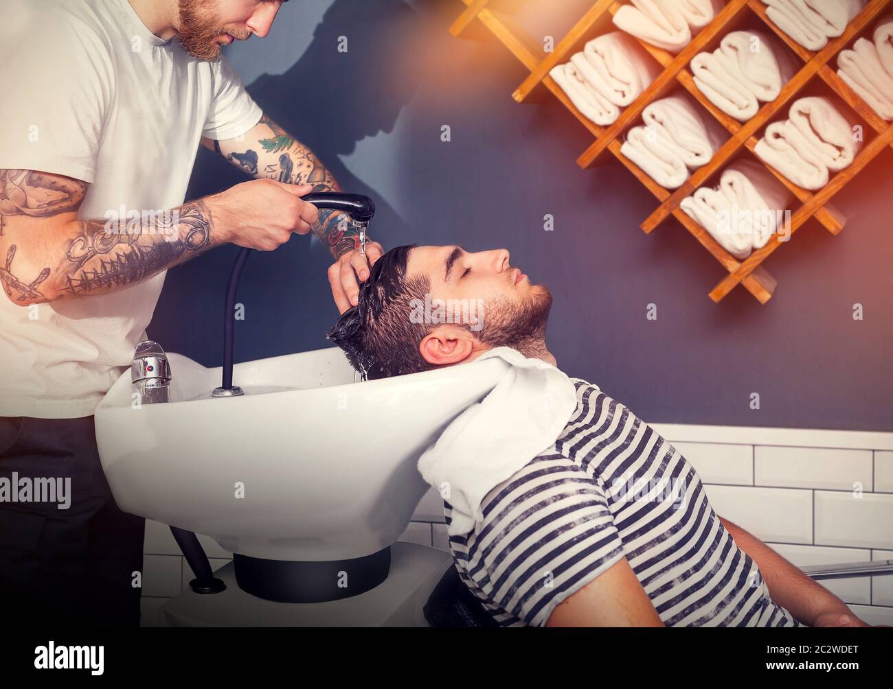 Young man has his hair washed in barber's shop, barber is washing the ...