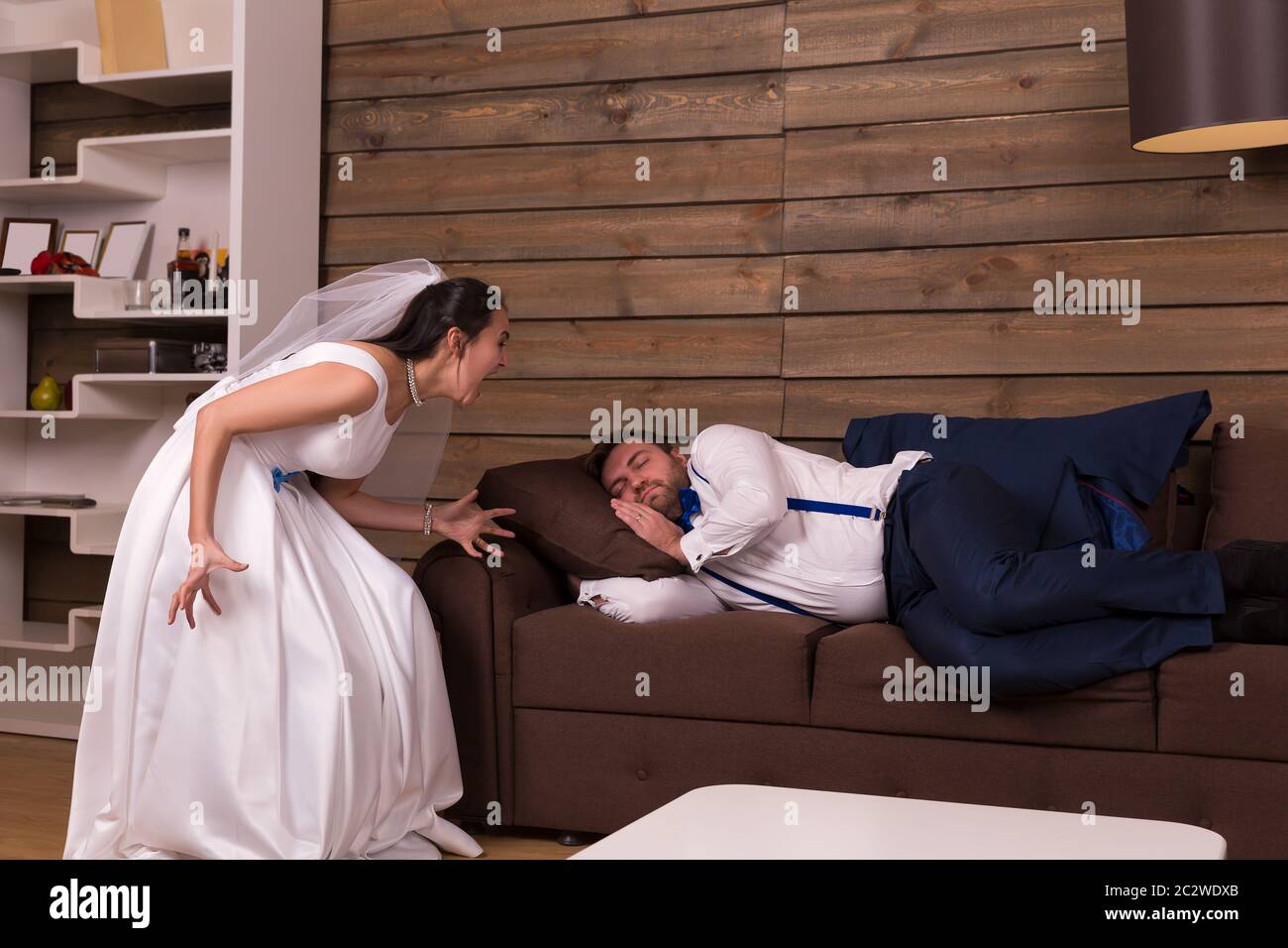 Bride in white dress and veil is shouting on a drunk sleeping on couch ...