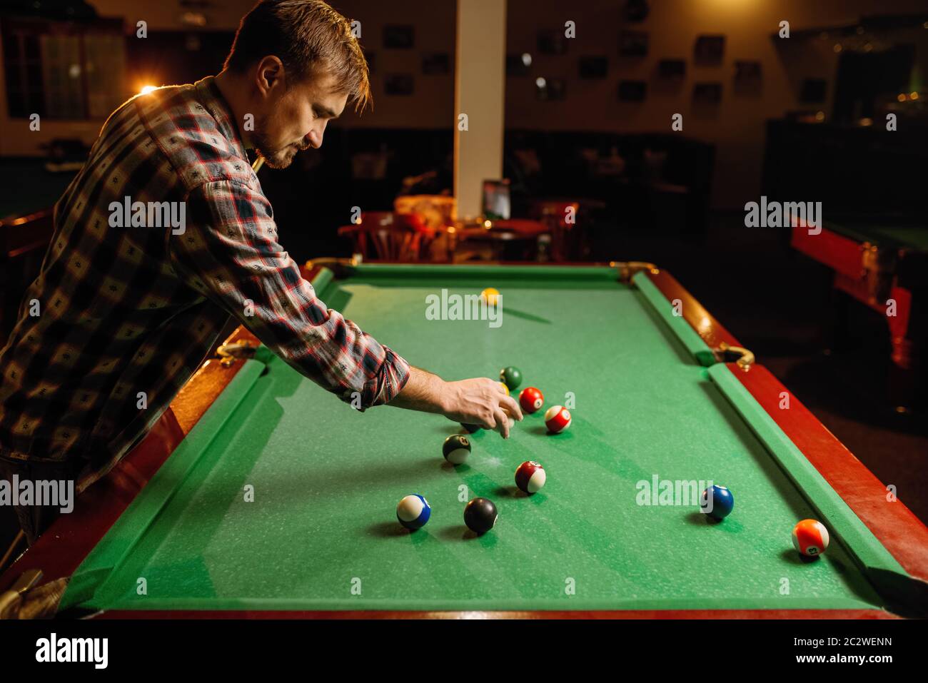 Male billiard player places balls on green table, poolroom interior on ...