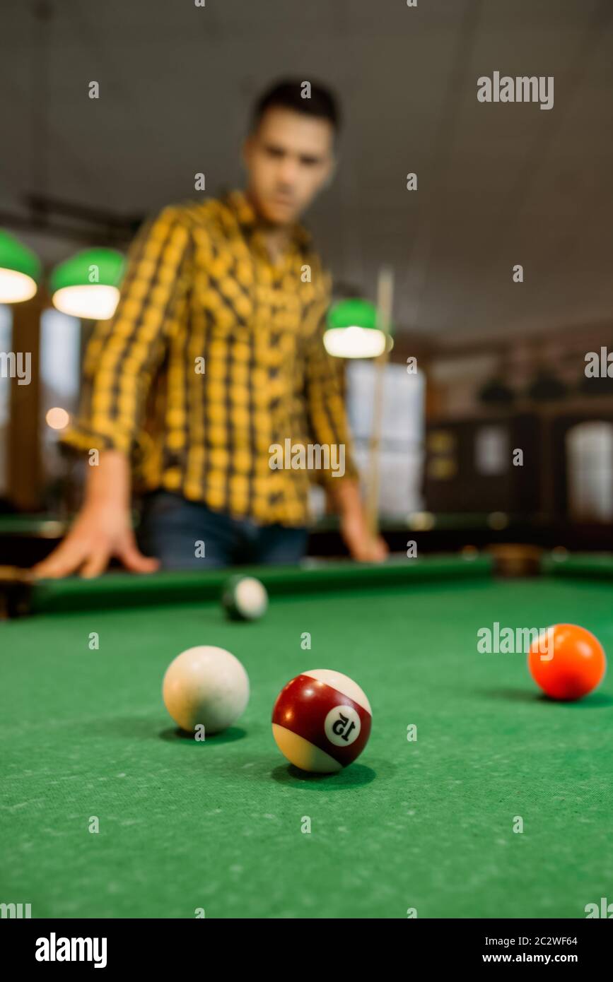 Male billiard player with cue, view from the table with colorful balls ...