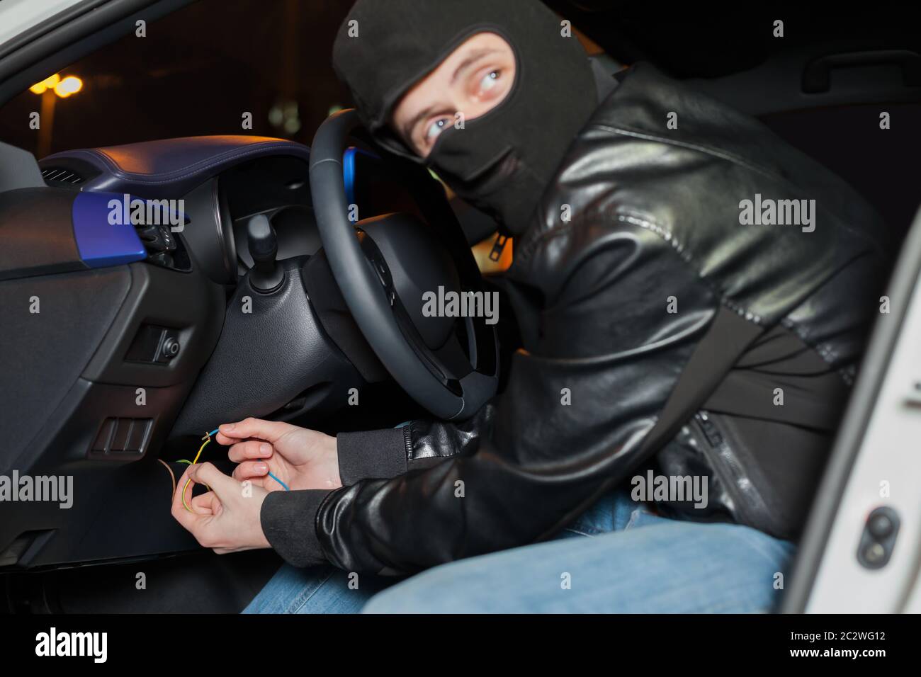 Male car thief breaks the ignition switch. Carjacker with balaclava on ...