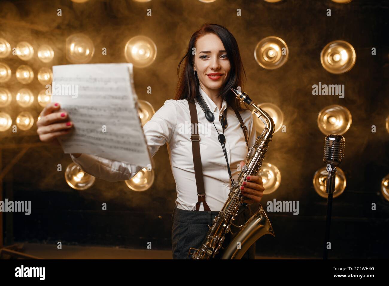 Female saxophonist with saxophone holds music book on the stage with ...