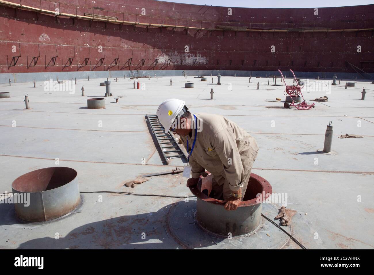 A supervisor steps through an hatch injto the lid of an oil tank ...
